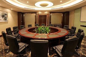 Uma sala de conferência com uma mesa redonda cercada por cadeiras, uma tela grande e um projetor.