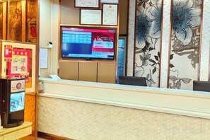 Uma área de recepção com painel digital, balcão e parede decorativa.
