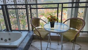 Uma varanda com mesa de vidro, duas cadeiras de vime, um vaso de plantas e uma banheira.