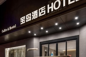 Entrada de hotel com uma placa em chinês e inglês, um balcão de recepção e uma porta de vidro.