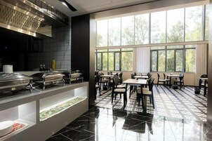 Restaurante com buffet, amplas janelas e piso ladrilhado.