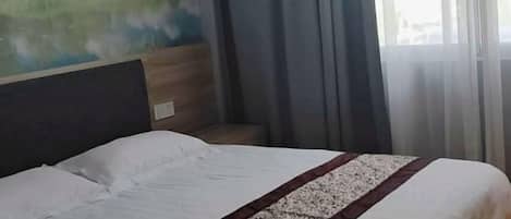 Quarto de hotel com cama, cabeceira, janela com cortinas e um mural na parede.