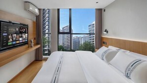 Quarto de hotel com uma cama grande, uma TV em uma estante de madeira e vista para edifícios altos.