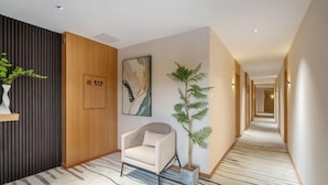 Um lobby de hotel moderno com uma mesa de recepção de madeira, uma área de estar com uma poltrona, um quadro abstrato grande e um vaso de planta.