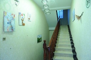Escadaria com corrimão de madeira, parede estampada e obras de arte.