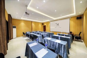 Uma sala de conferências com mesas, cadeiras, um projetor e tela de apresentação.