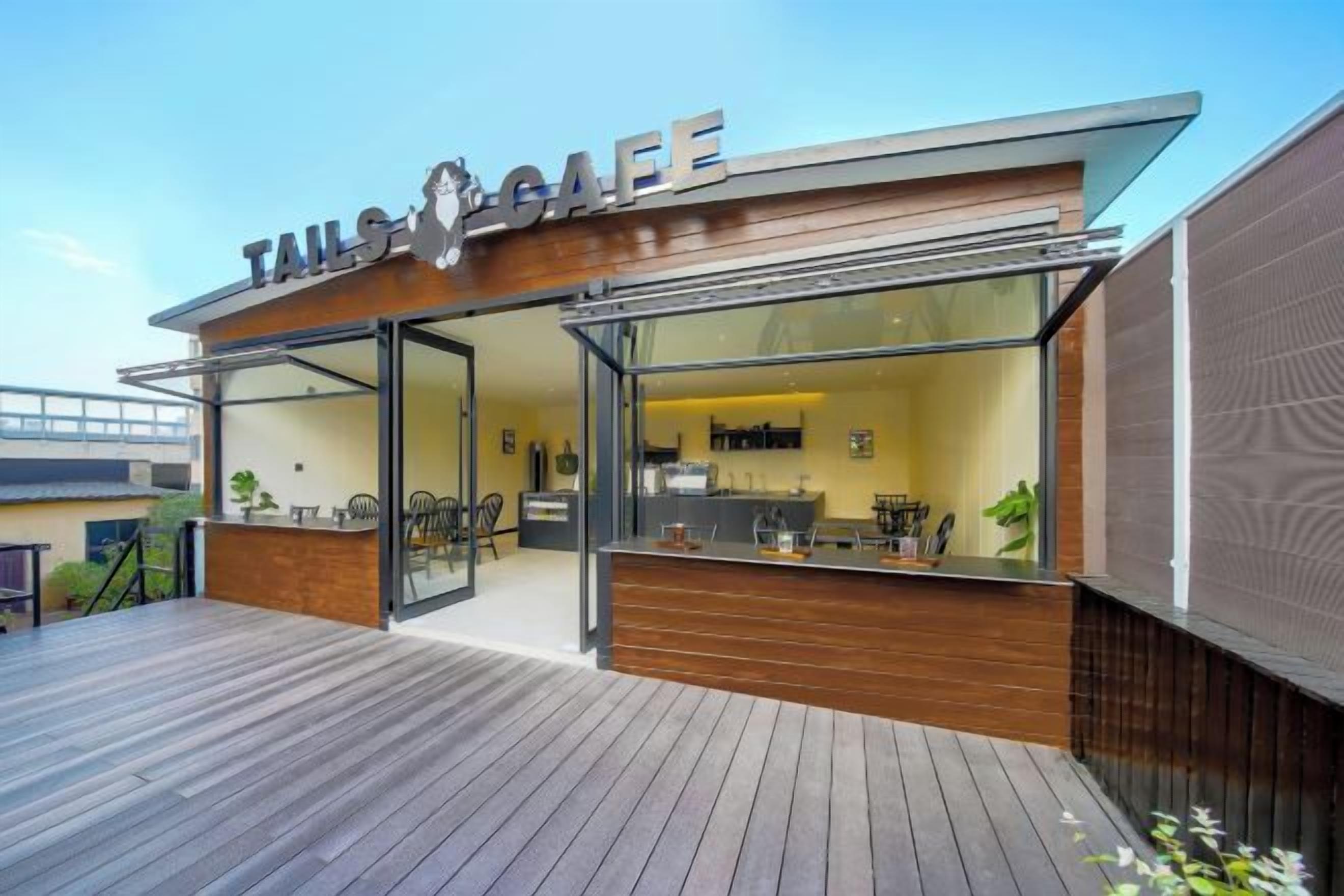 Um café moderno com terraço de madeira, entrada de vidro e cozinha à vista.