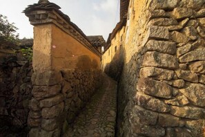 Um caminho de pedra estreito, ladeado por muros de pedra antigos, que conduz a um edifício com telhado tradicional.