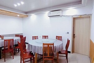 Sala de conferências com mesas e cadeiras redondas, um aparelho de ar condicionado e uma porta de madeira.
