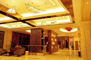 Um saguão de hotel com design moderno, apresentando uma coluna central, área de estar e um balcão de recepção.