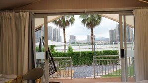 Quarto com cama, poltrona e vista para a cidade através de grandes janelas.