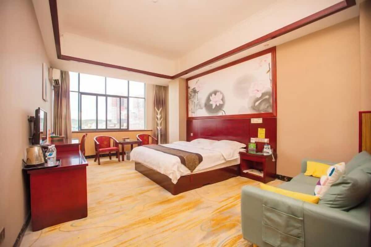 Quarto de hotel com cama, escrivaninha, cadeira, sofá e um quadro na parede.