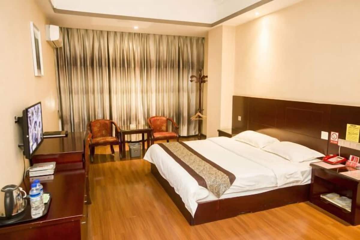 Quarto de hotel com uma cama grande, uma mesa com cadeira, uma televisão e um cabideiro.
