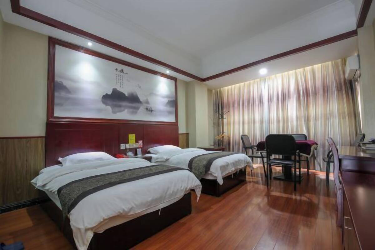 Quarto de hotel com duas camas, uma escrivaninha, uma cadeira e um quadro grande na parede.
