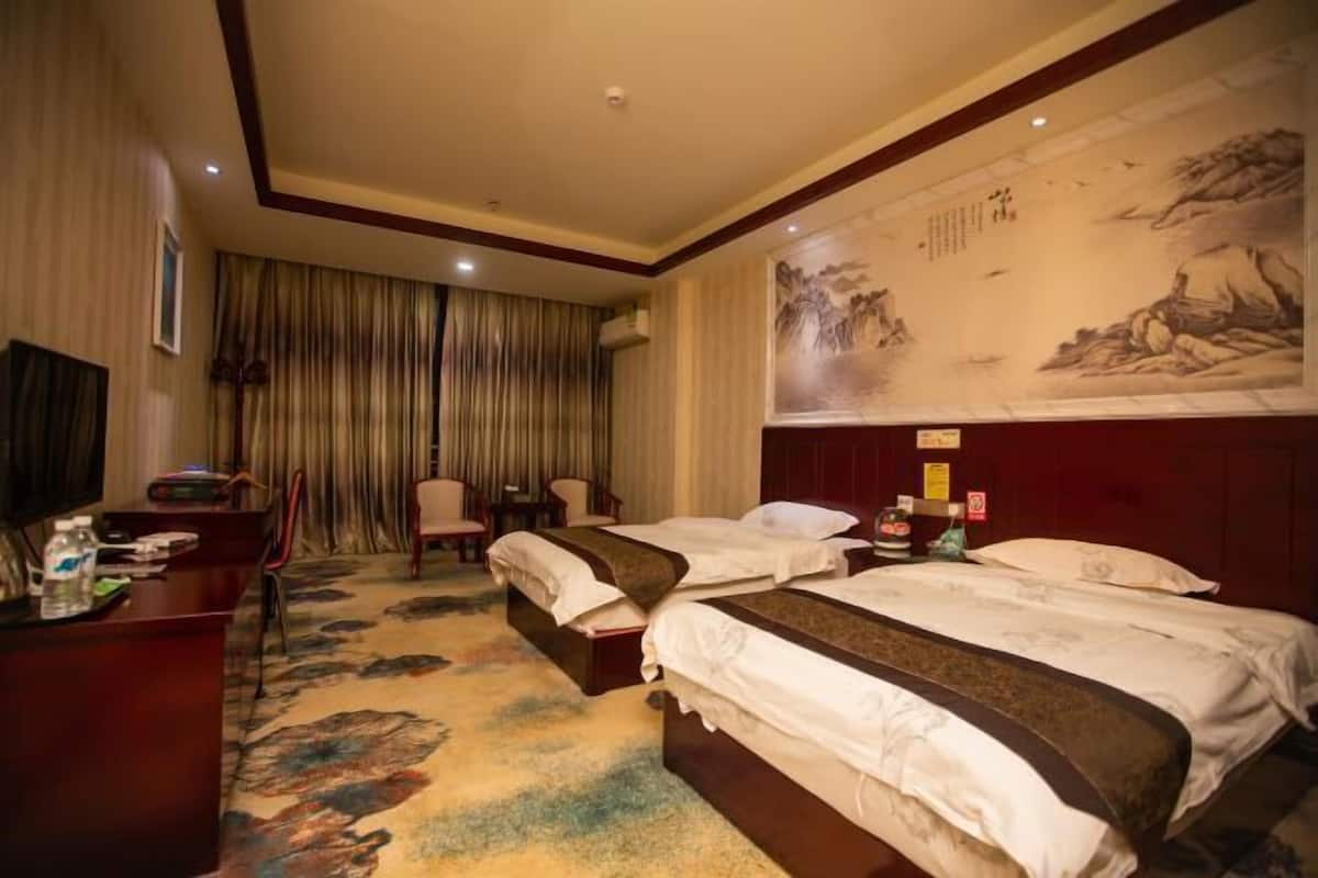 Quarto de hotel com duas camas, uma escrivaninha, cadeiras e uma pintura grande na parede.