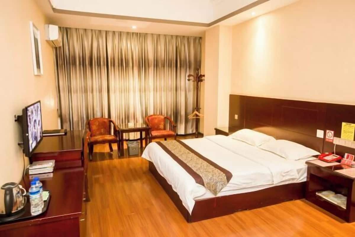 Quarto de hotel com cama, escrivaninha com cadeira, televisão e cabideiro.
