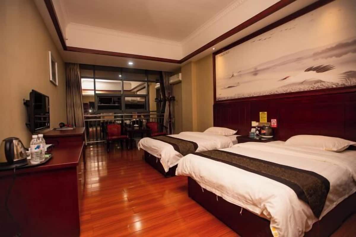 Quarto de hotel com duas camas, uma escrivaninha, uma cadeira, televisão e um quadro na parede.