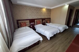 Quarto de hotel com três camas de solteiro, cabeceiras de madeira e papel de parede estampado na parede.