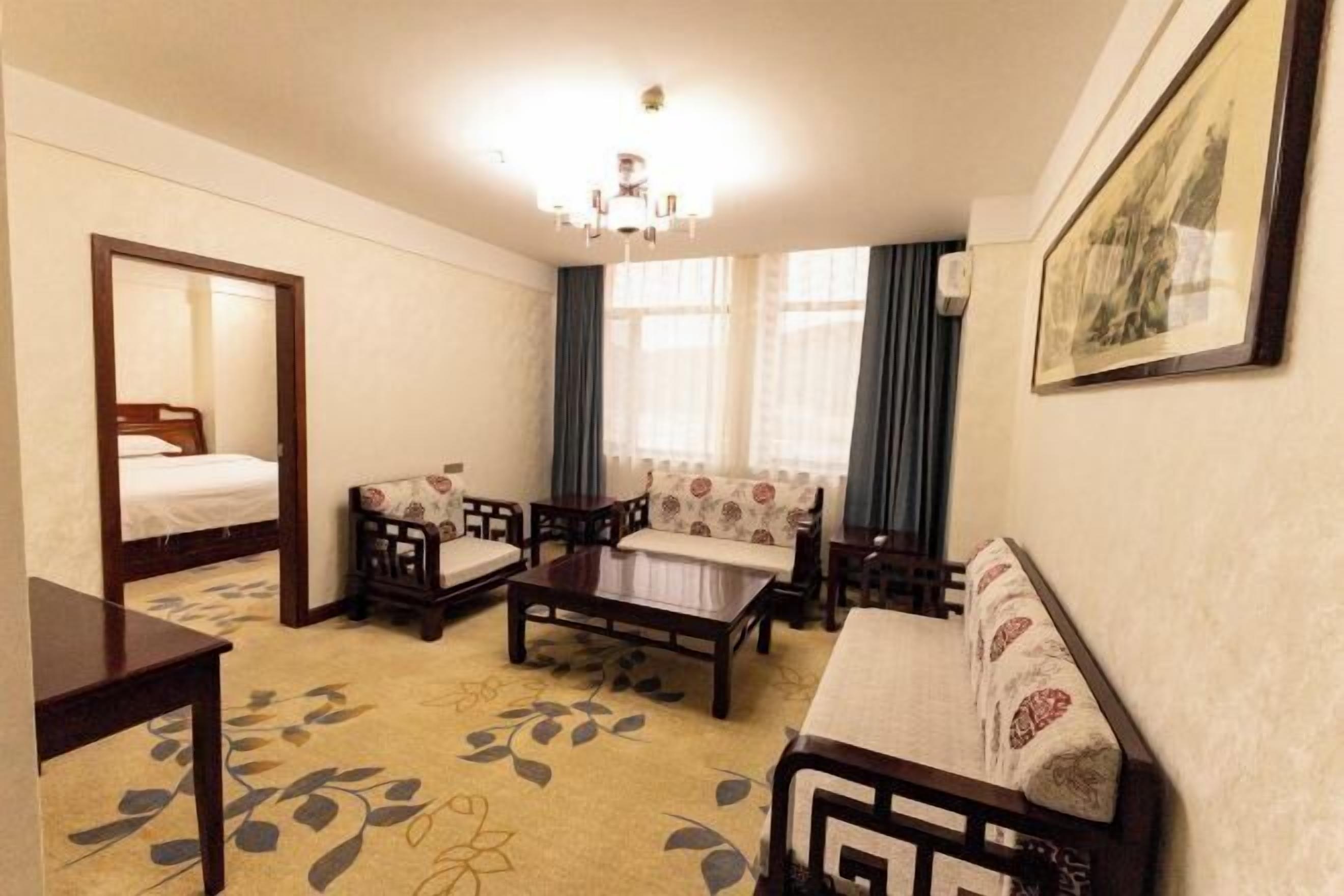 Quarto de hotel com cama, dois sofás, mesa de centro e lustre.