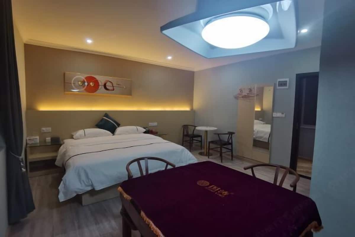Quarto de hotel com cama, escrivaninha, cadeira, mesinha, espelho e luminária de teto.