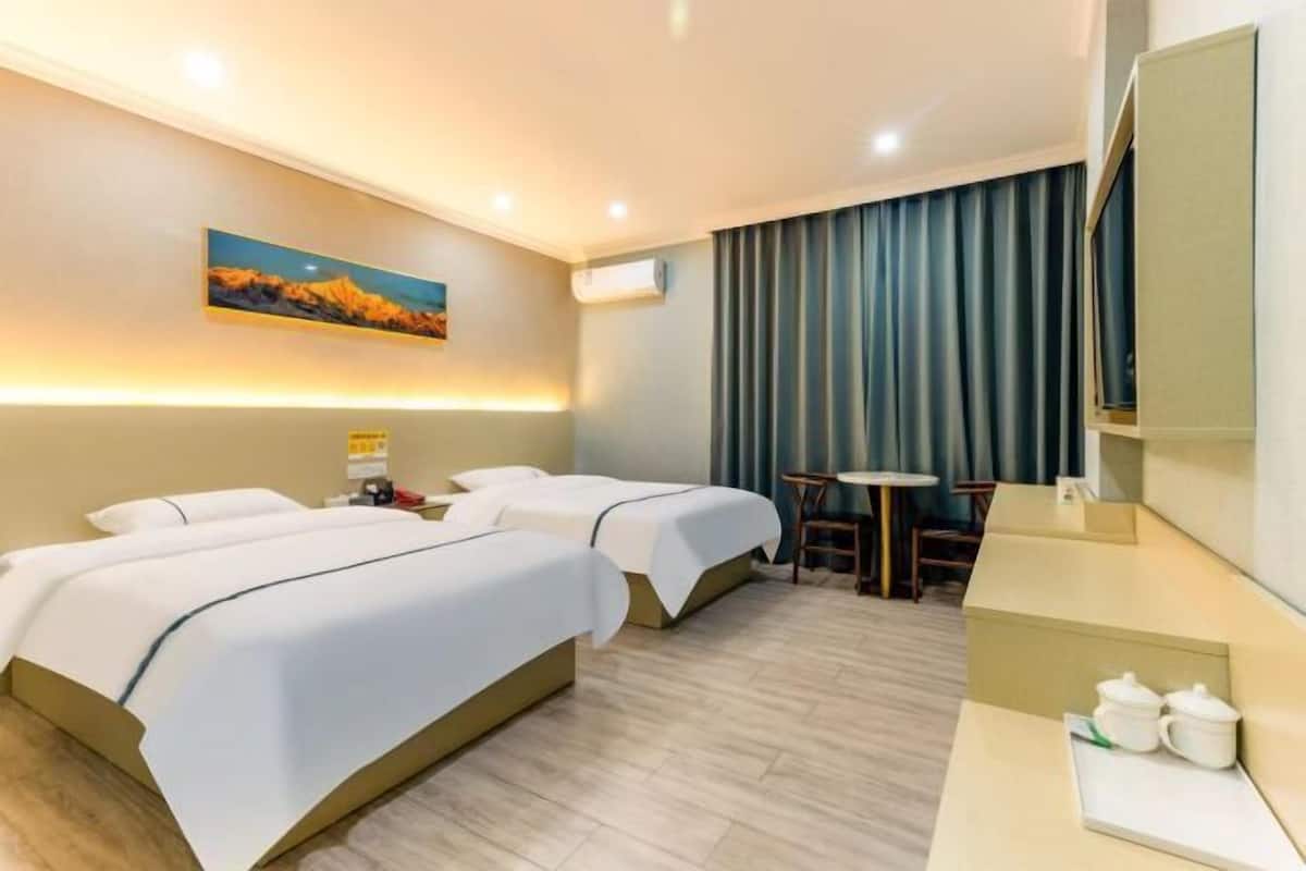 Quarto de hotel com duas camas, uma escrivaninha, uma cadeira, uma mesa pequena, um quadro na parede e um espelho.