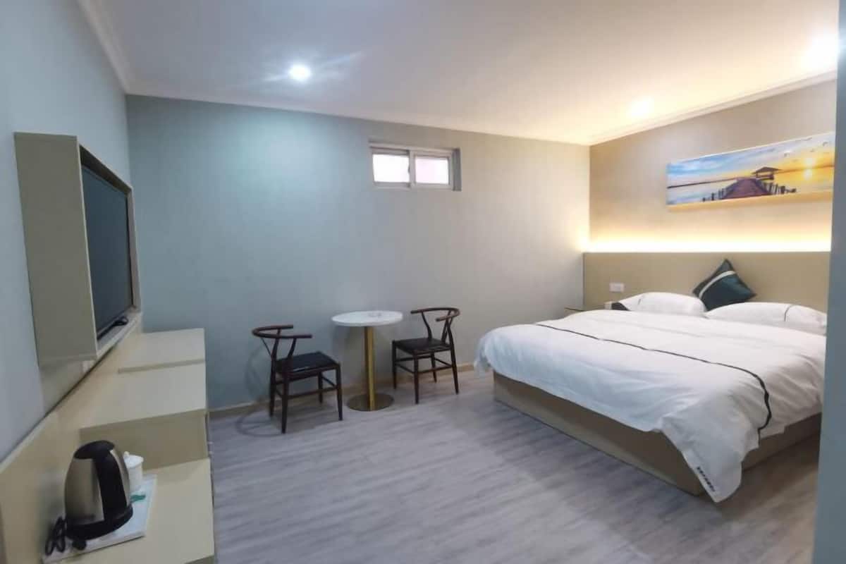 Quarto de hotel com cama, televisão, mesa pequena, duas cadeiras, cafeteira e um quadro na parede.