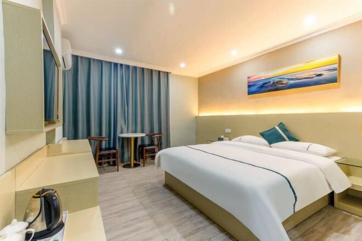Quarto de hotel com cama, mesas de cabeceira, escrivaninha com cadeira, mesa redonda pequena e um quadro na parede.