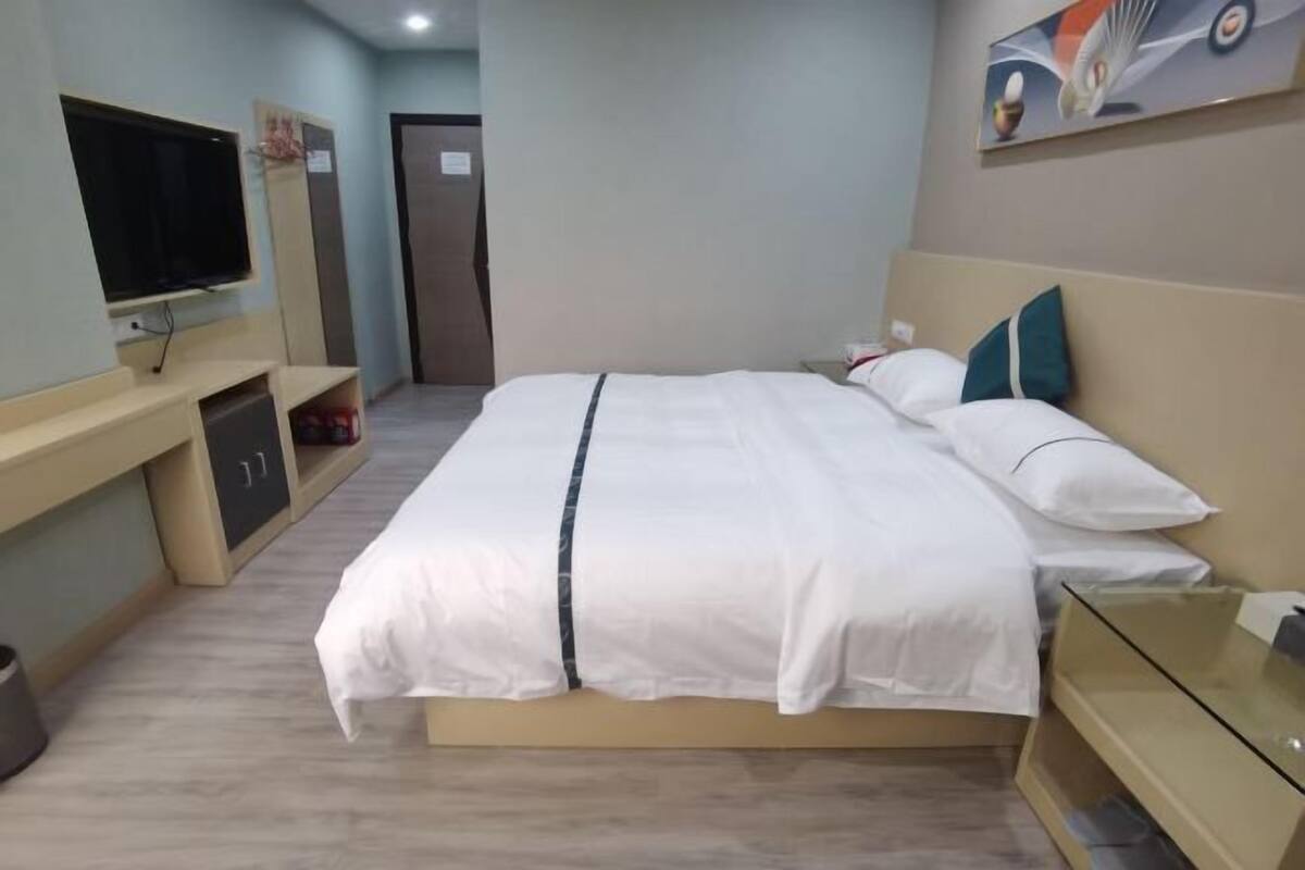 Quarto de hotel com cama, televisão, escrivaninha e porta.