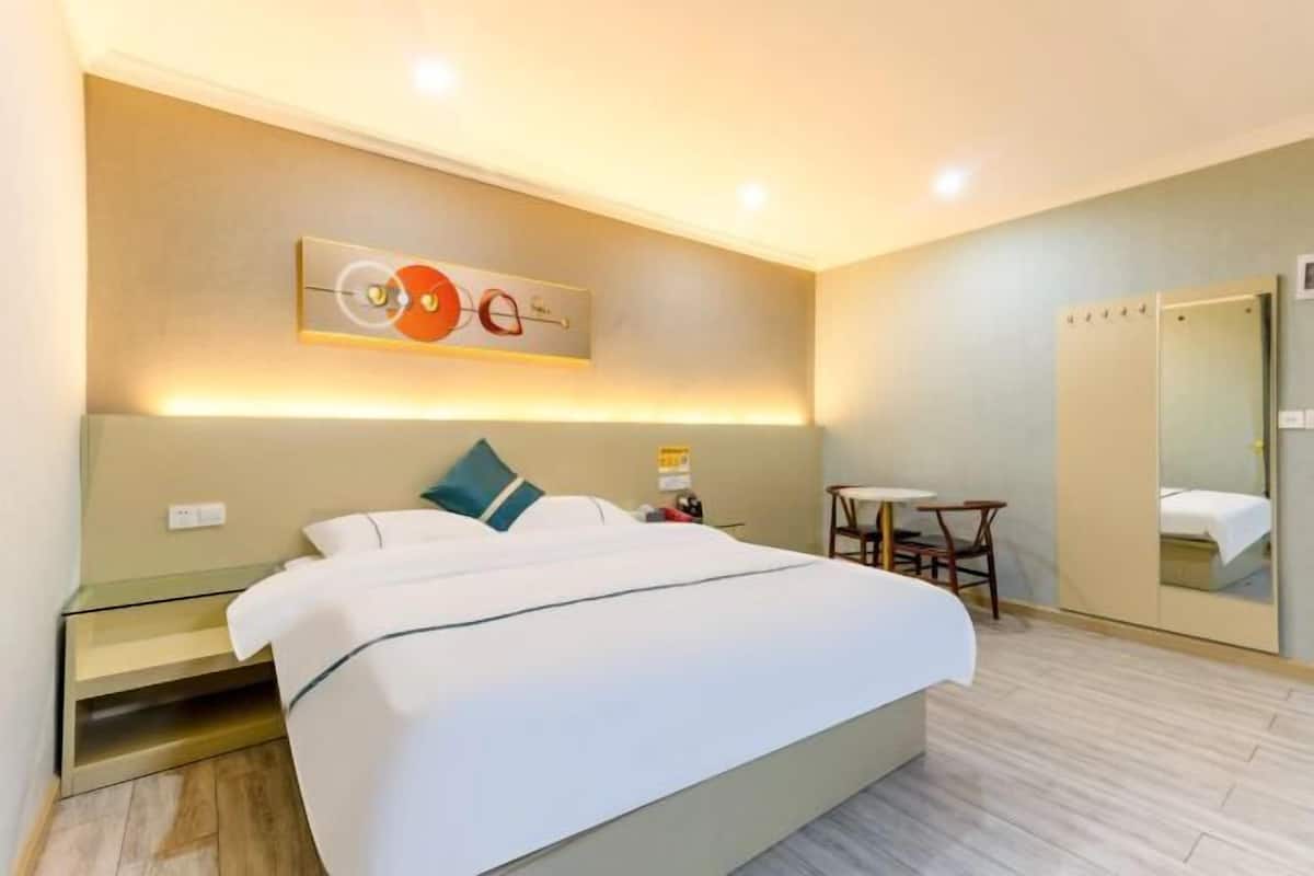 Quarto de hotel com cama, mesa de cabeceira, uma pequena mesa com cadeiras, um espelho e uma obra de arte na parede.