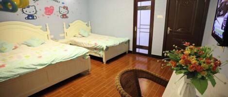 Quarto com duas camas, uma cadeira de vime, uma TV e um enfeite na parede.