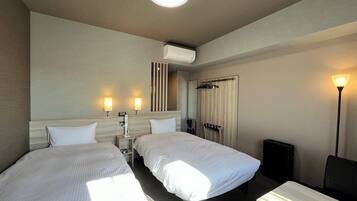 Quarto de hotel com duas camas de solteiro, uma mesinha de cabeceira, escrivaninha, cadeira, luminária e ar condicionado.