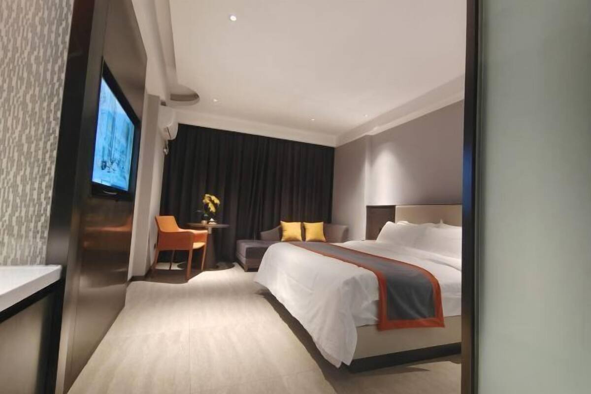 Quarto de hotel moderno com uma cama grande, uma escrivaninha com cadeira, televisão e vista para a cidade.
