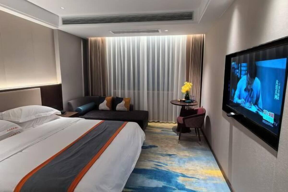 Quarto de hotel com cama, televisão, escrivaninha e cadeira.
