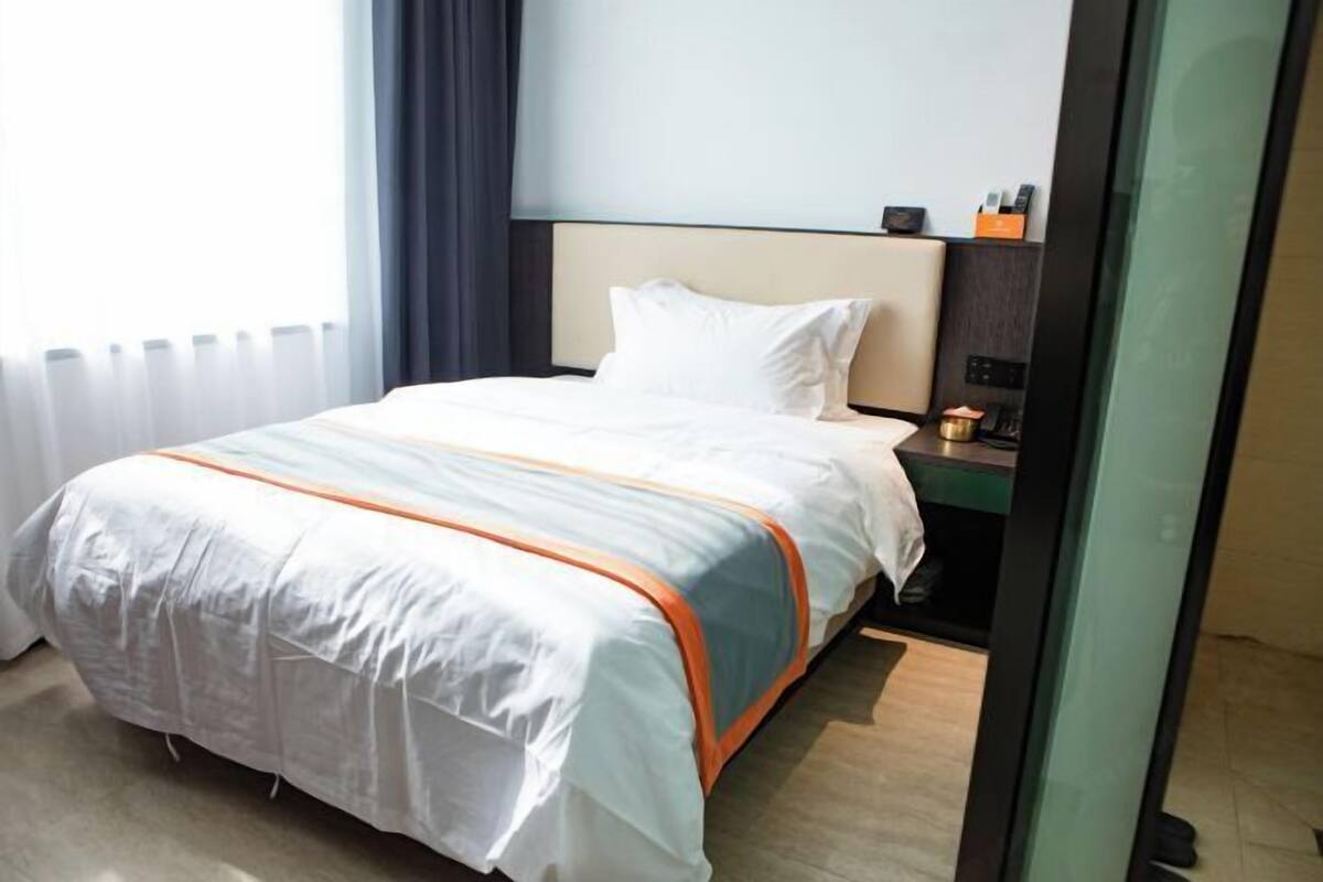 Quarto de hotel com cama, mesa de cabeceira e janela com cortinas.