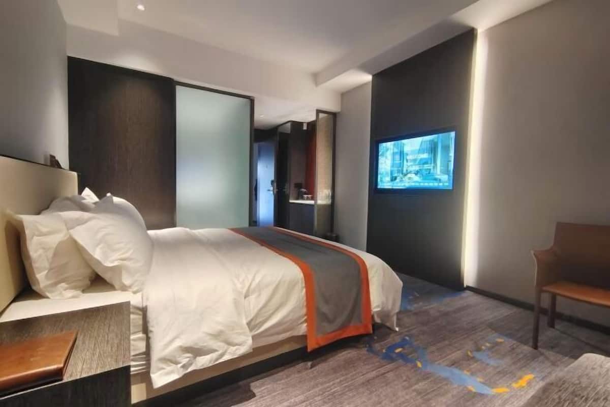 Quarto de hotel moderno com uma cama grande, uma escrivaninha e uma televisão na parede.