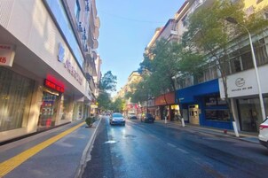 Rua com lojas, asfalto molhado e carros estacionados.
