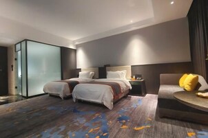 Quarto de hotel moderno com duas camas, um sofá e um painel de vidro.