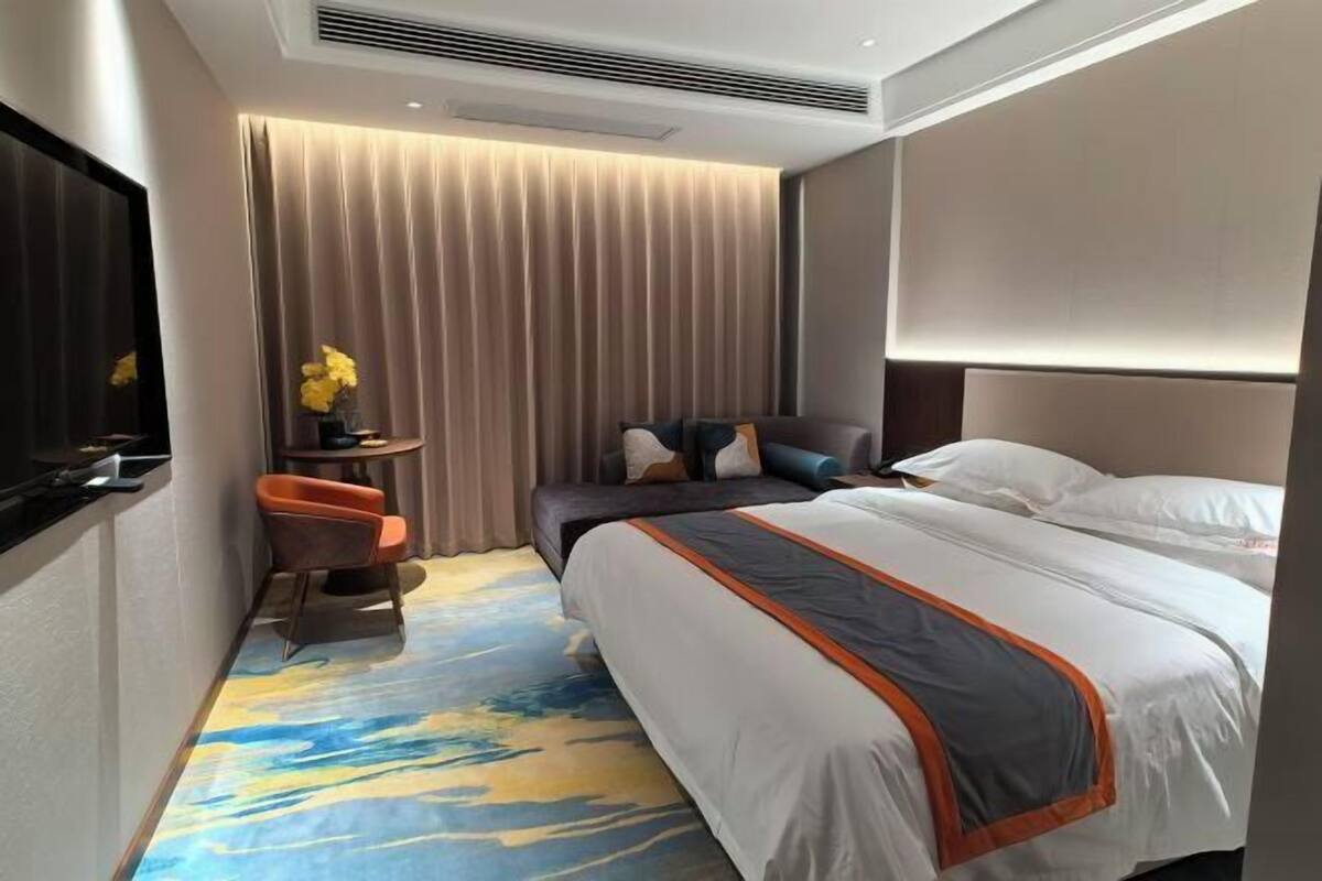 Quarto de hotel moderno com uma cama grande, área de estar com uma poltrona e uma pequena mesa com um vaso de flores.