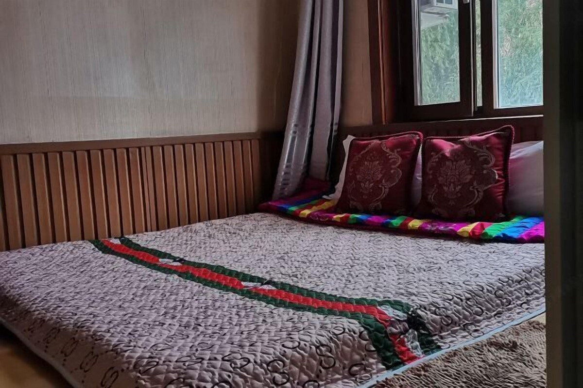 Uma cama com colcha estampada, duas almofadas vermelhas e um cobertor colorido.