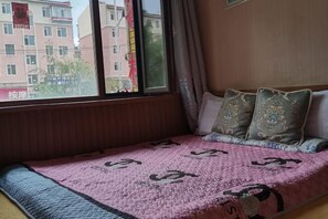 Quarto com cama, janela e vista para prédios.
