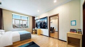 Quarto de hotel com cama, escrivaninha, cadeira, mesa pequena, janela grande e um quadro na parede.