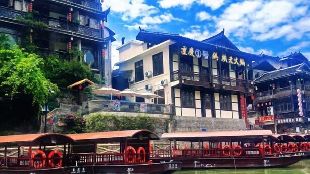 Um edifício tradicional com um letreiro em caracteres chineses, um canal com barcos e um céu claro.