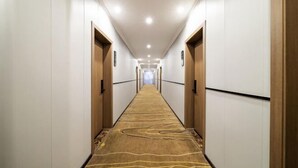 Um corredor de hotel com piso em carpete, portas de madeira e paredes brancas.