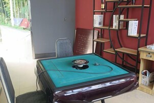 Uma mesa de bilhar com superfície de feltro verde e faixa de feltro vermelha, rodeada por uma parede vermelha com uma estante de metal preta.