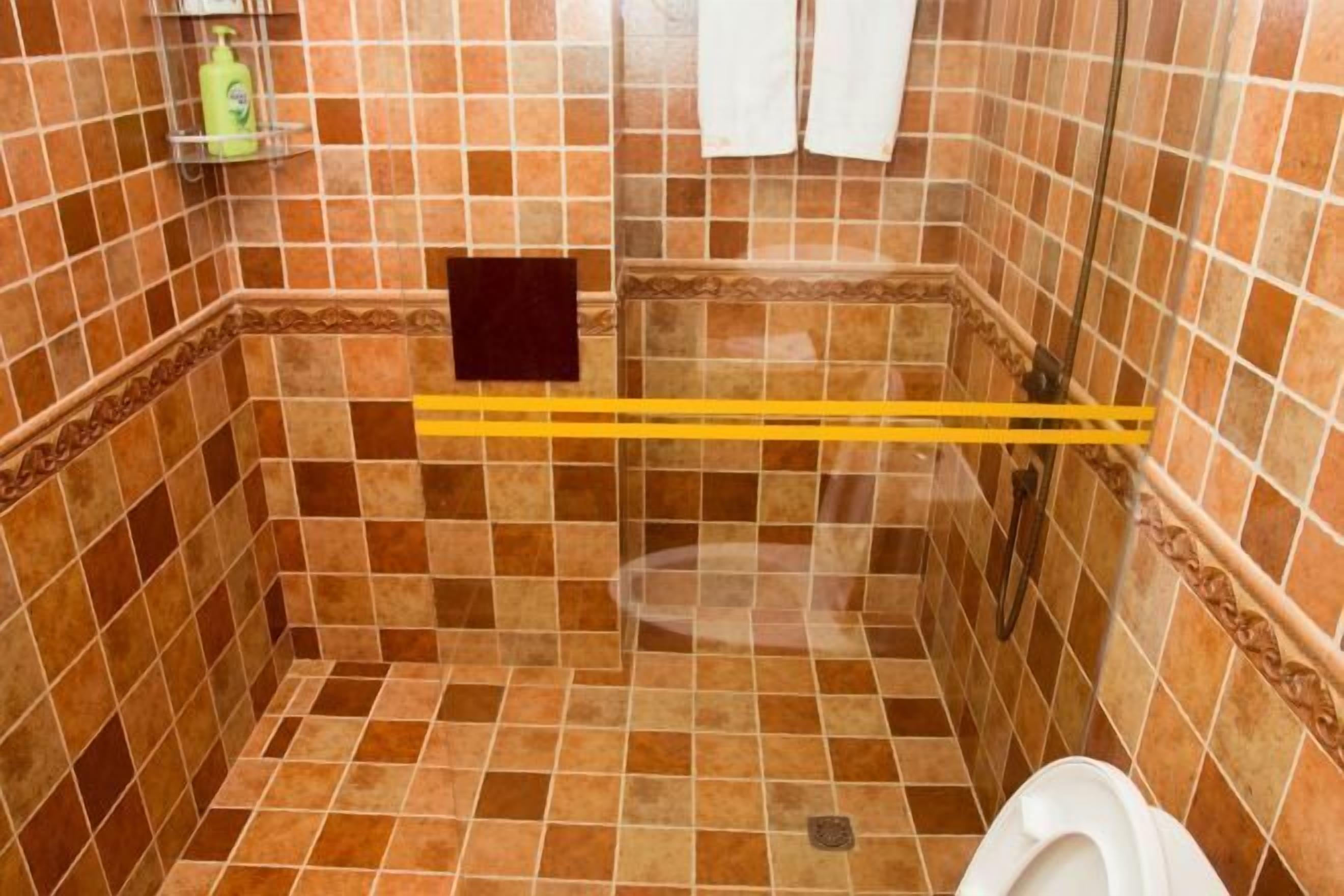 Um banheiro pequeno revestido com azulejos, com chuveiro, vaso sanitário e um prateleira com produtos de higiene.