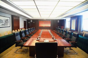 Uma sala de conferências com uma mesa comprida, cadeiras e tela de projeção.