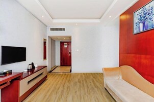 Quarto de hotel moderno com piso de madeira, parede em tom de vermelho, sofá bege, TV de tela plana e porta vermelha.