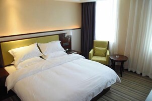 Quarto de hotel com uma cama grande, uma mesa de cabeceira, uma luminária, uma cadeira e uma pequena mesa.