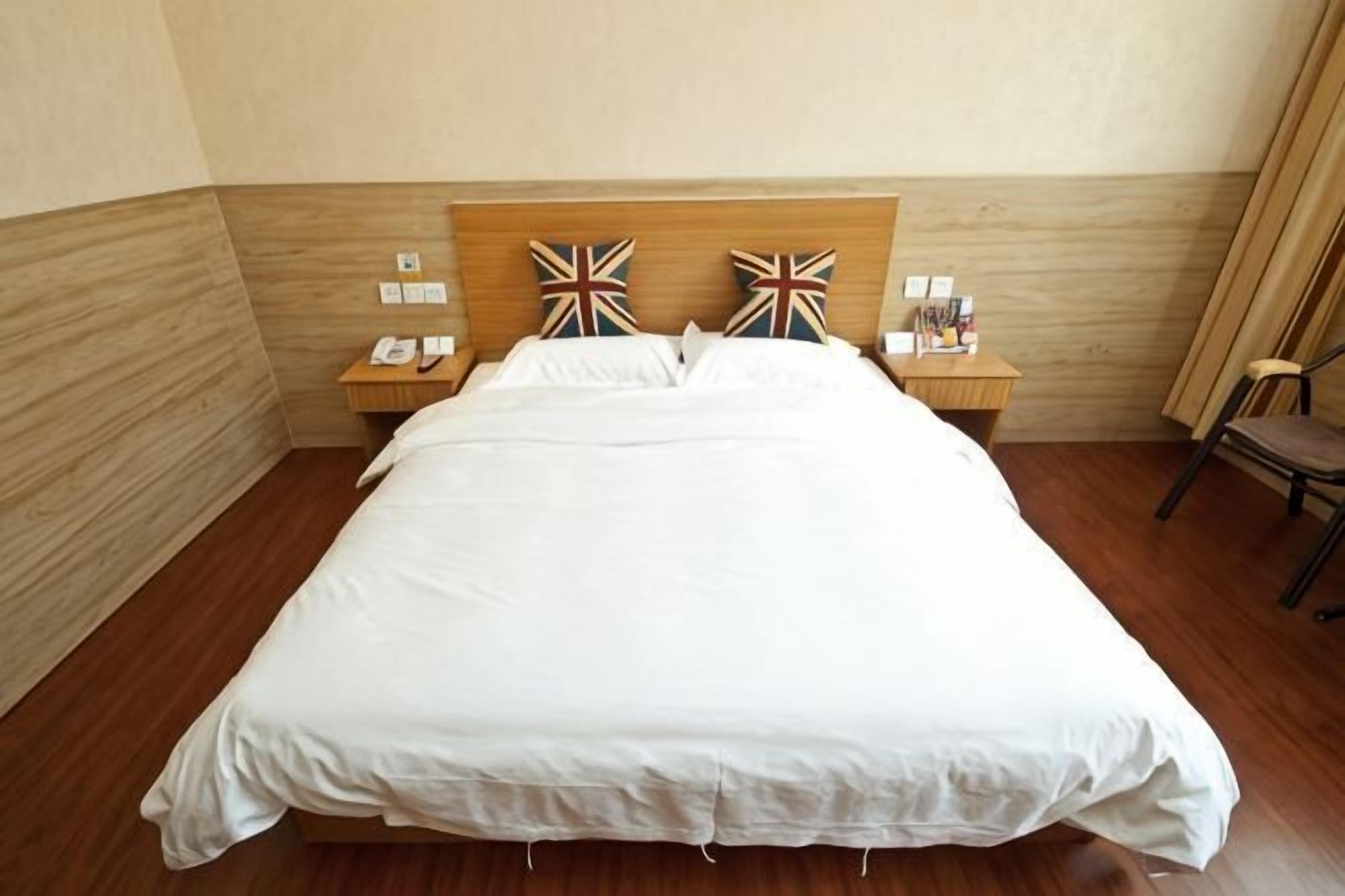 Uma cama bem arrumada com cabeceira de madeira, duas mesas de cabeceira com abajures e uma cadeira.
