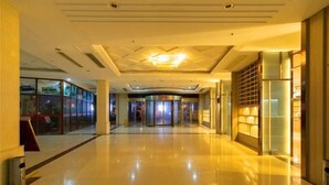 Um hall de hotel espaçoso e bem iluminado, com piso brilhante, um candelabro central e portas de vidro que dão para a entrada.